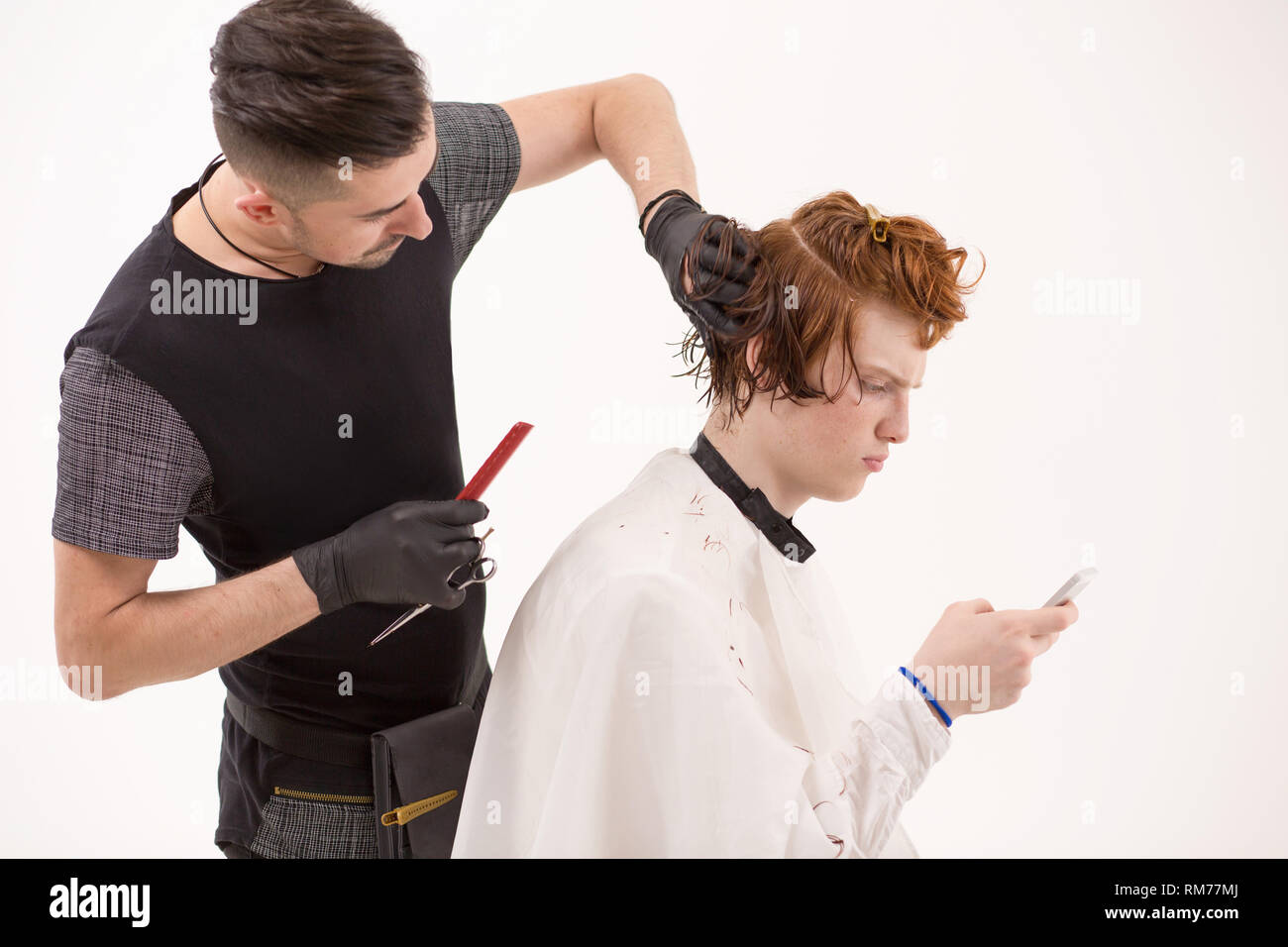 Handsome ginger man browsing at his phone, while getting a haircut ...