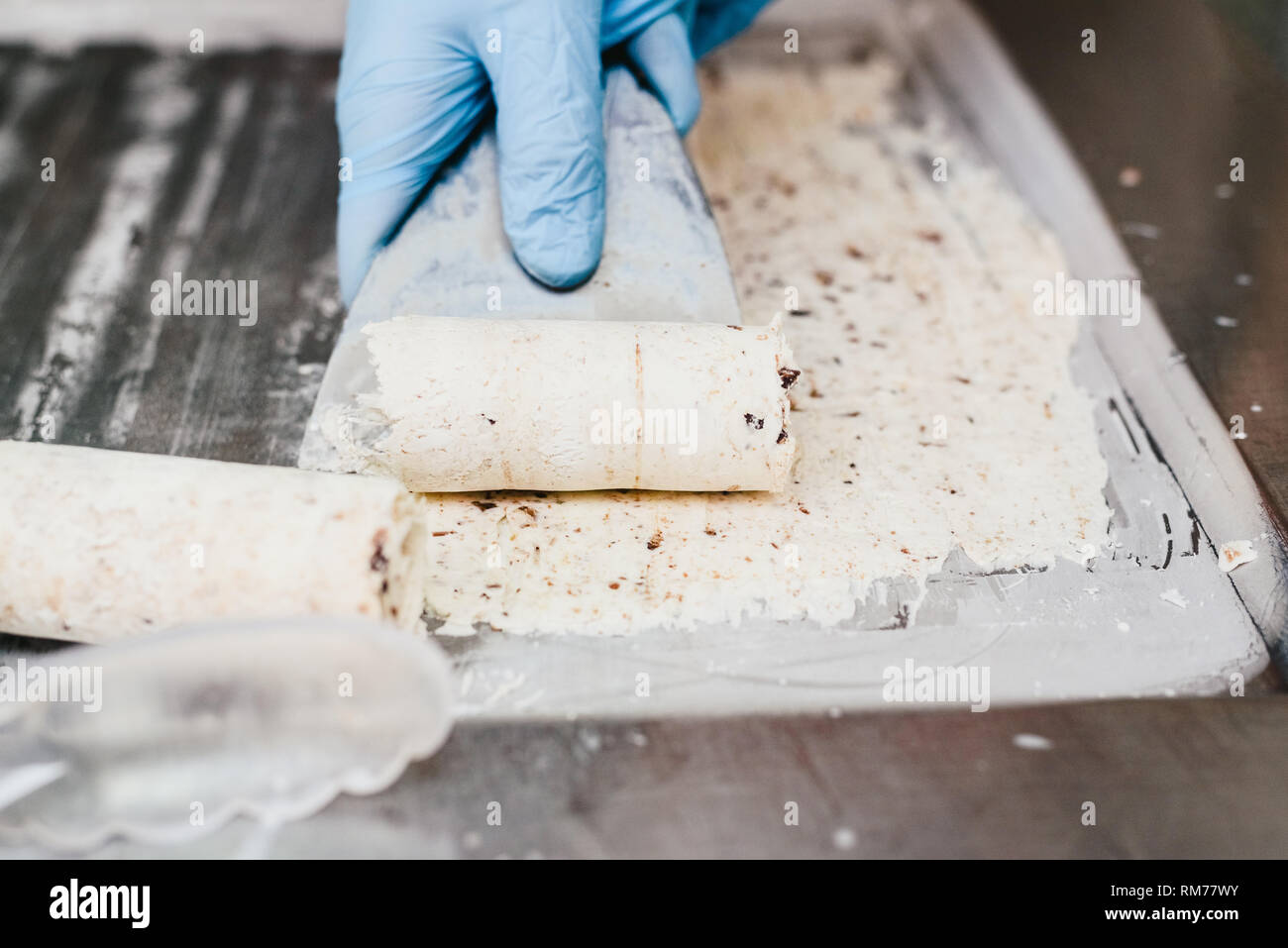 Rolling a white ice cream to prepare a cup of chocolate-wrapped ice ...
