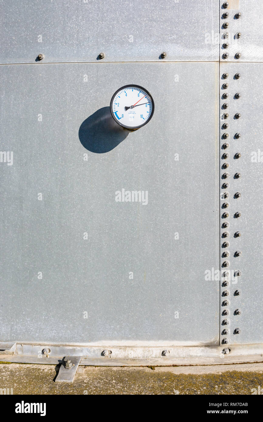 A round gauge fitted on the wall of a large galvanized steel water tank ...