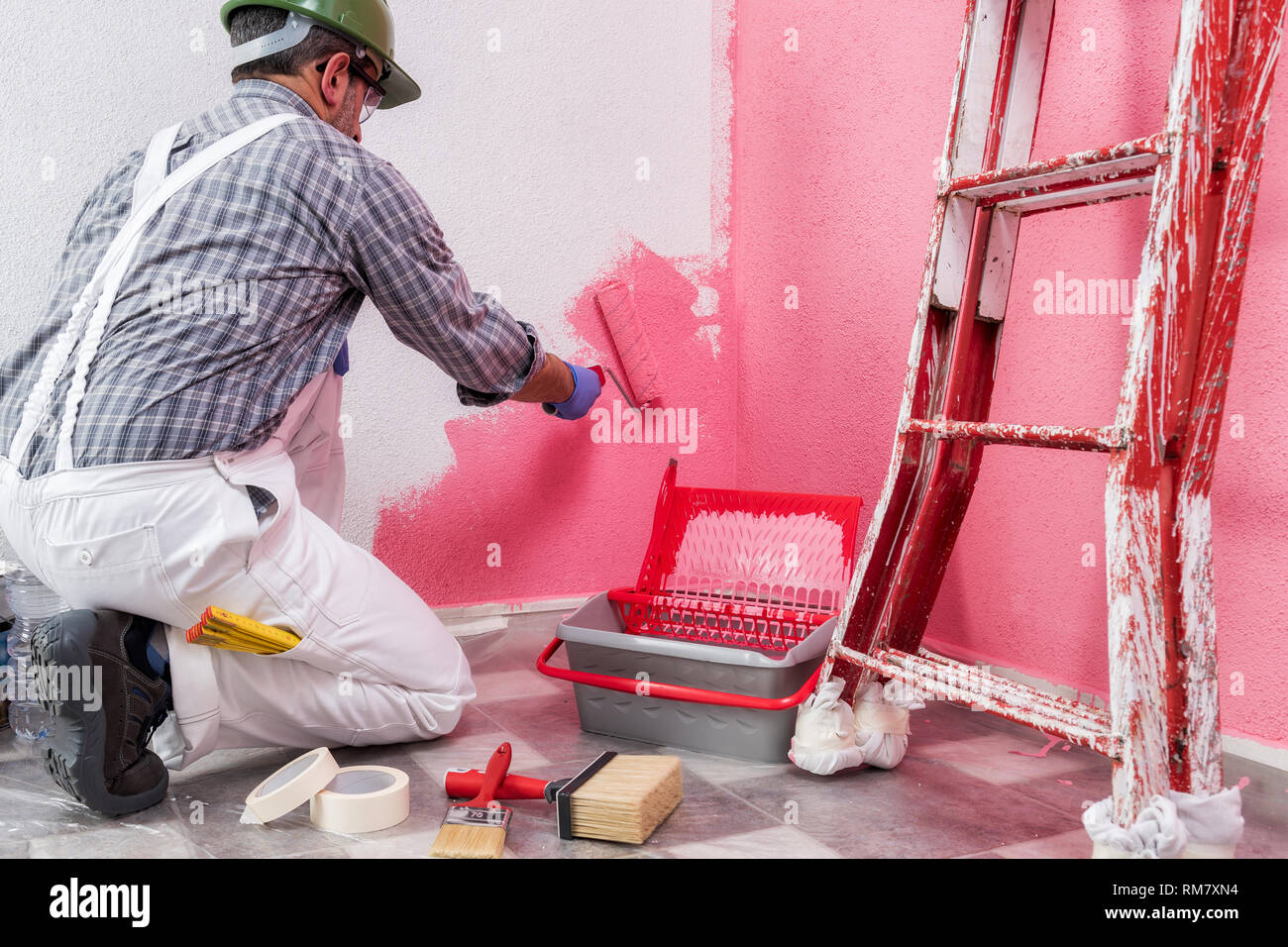 Caucasian house painter worker in white work overalls, with the roller ...