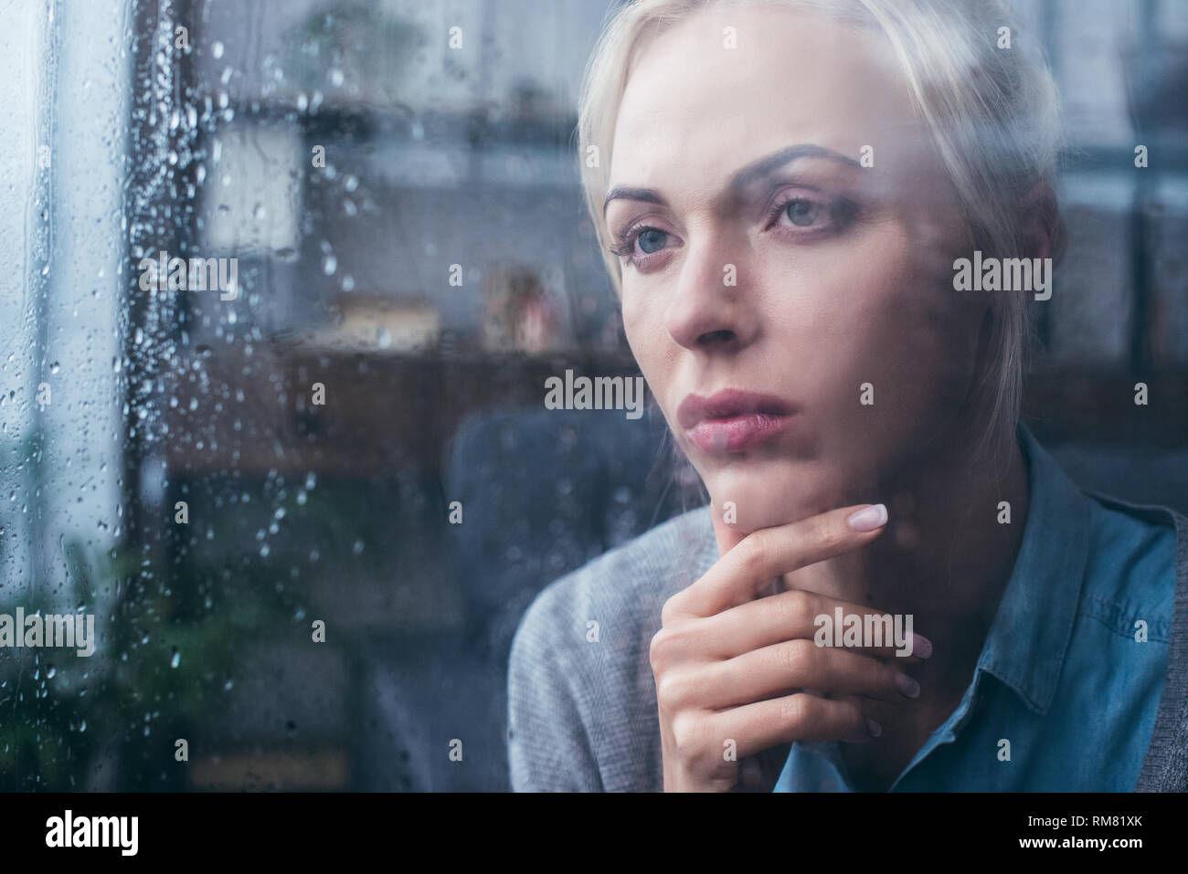 sad thoughtful adult woman touching face at home through window with ...