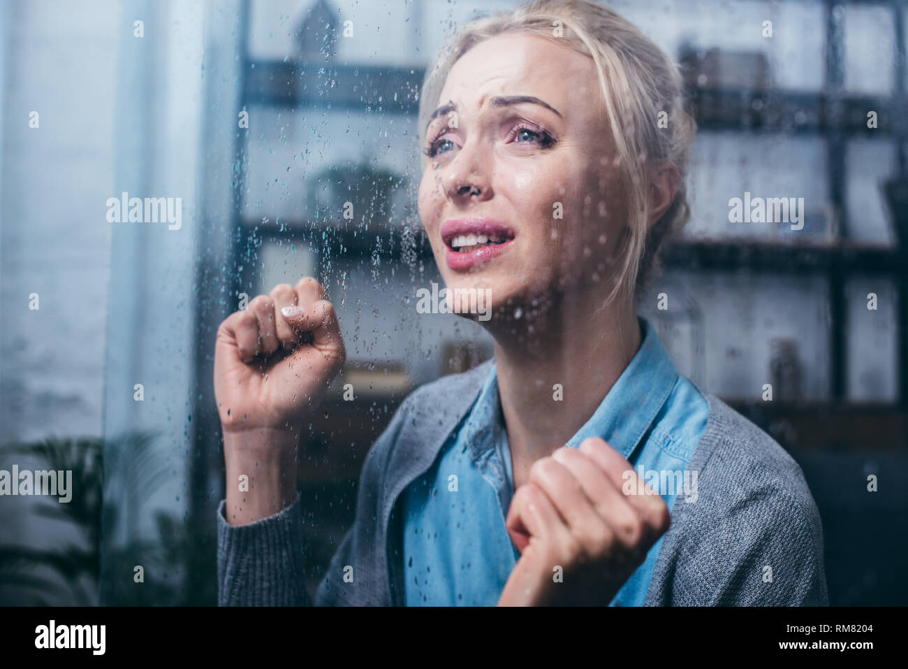sad adult woman crying with clenched fists at home through window with ...