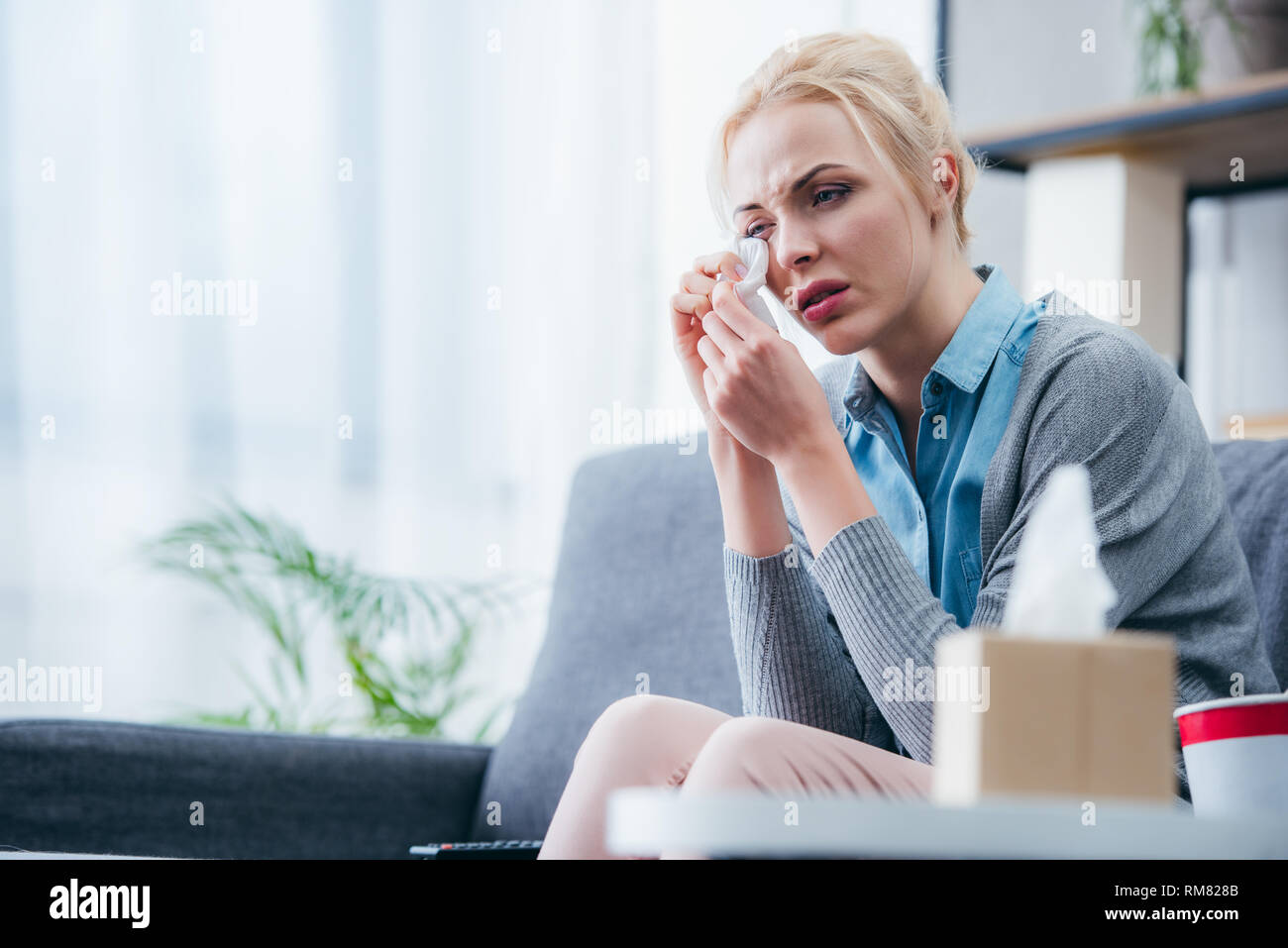 selective focus of upset woman crying and wiping tears on couch at home ...