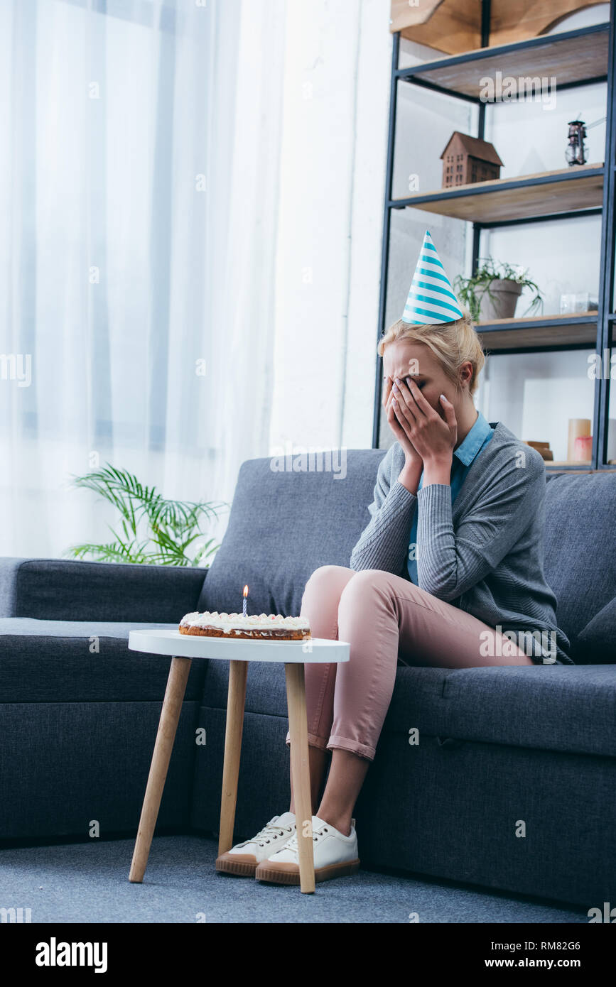 upset woman in party hat crying while celebrating birthday at home ...