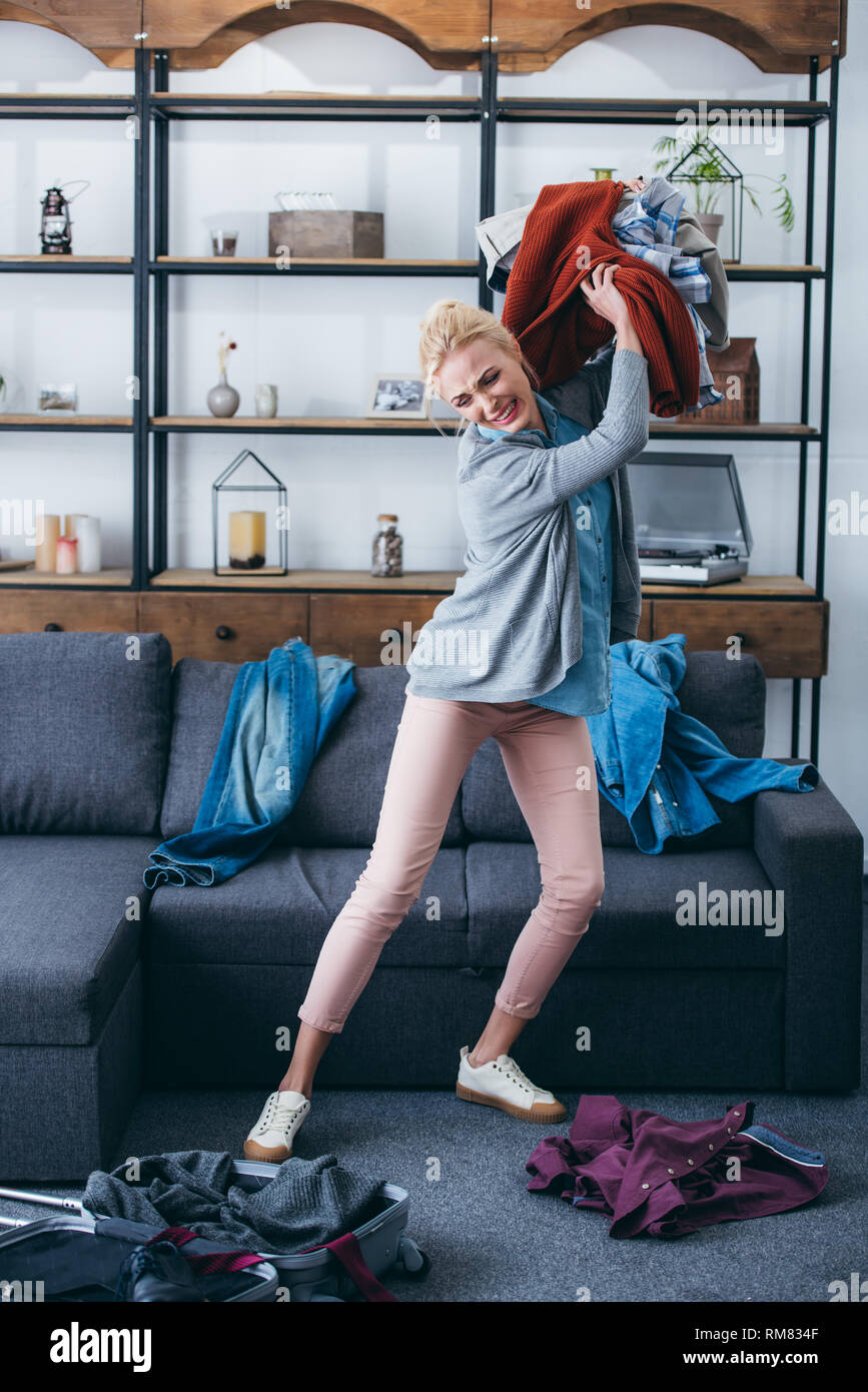 irritated woman throwing clothes in living room after breaking up with ...