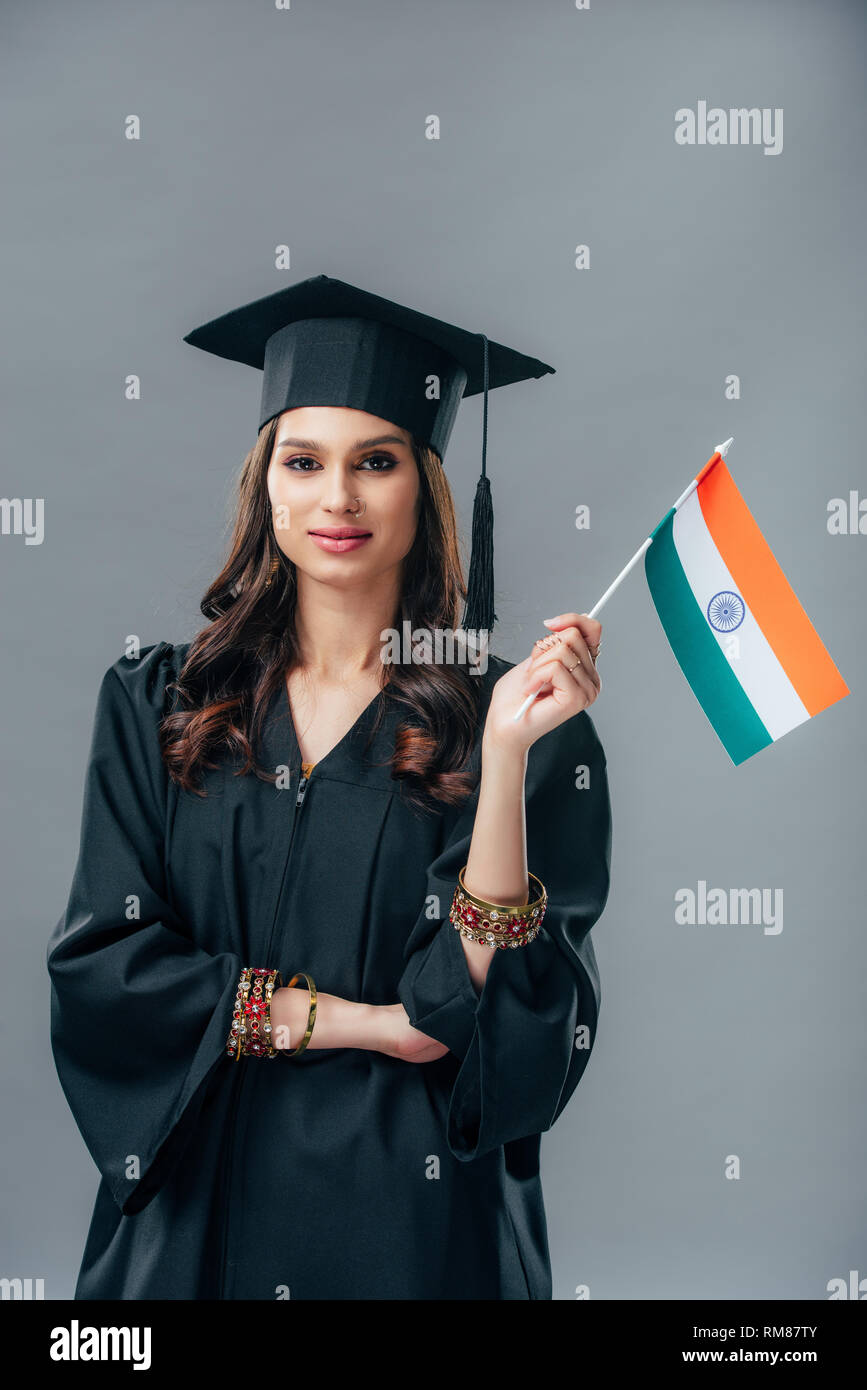 elegant indian student in academic gown and graduation cap holding ...