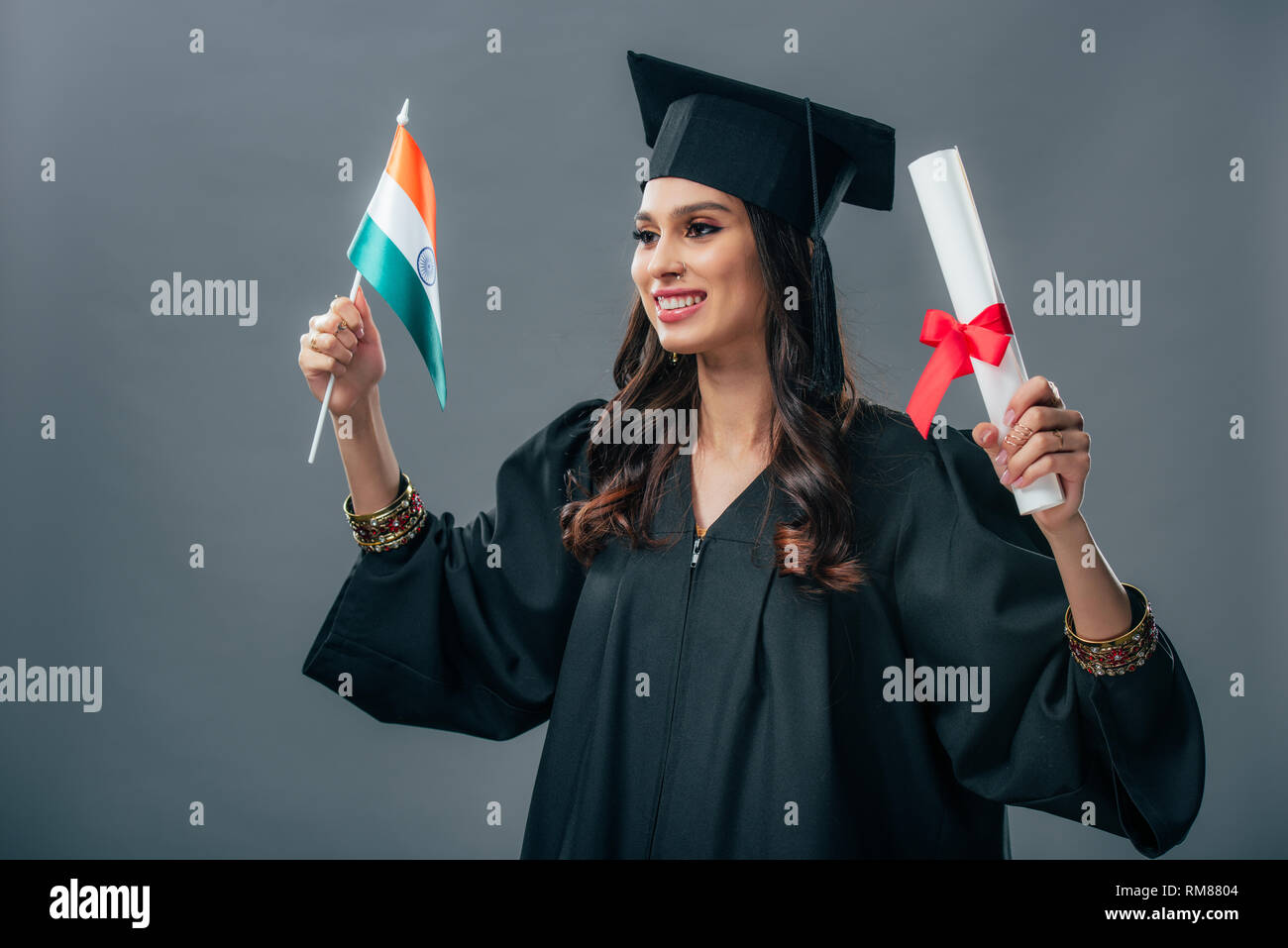 female indian student in academic gown and graduation cap holding ...