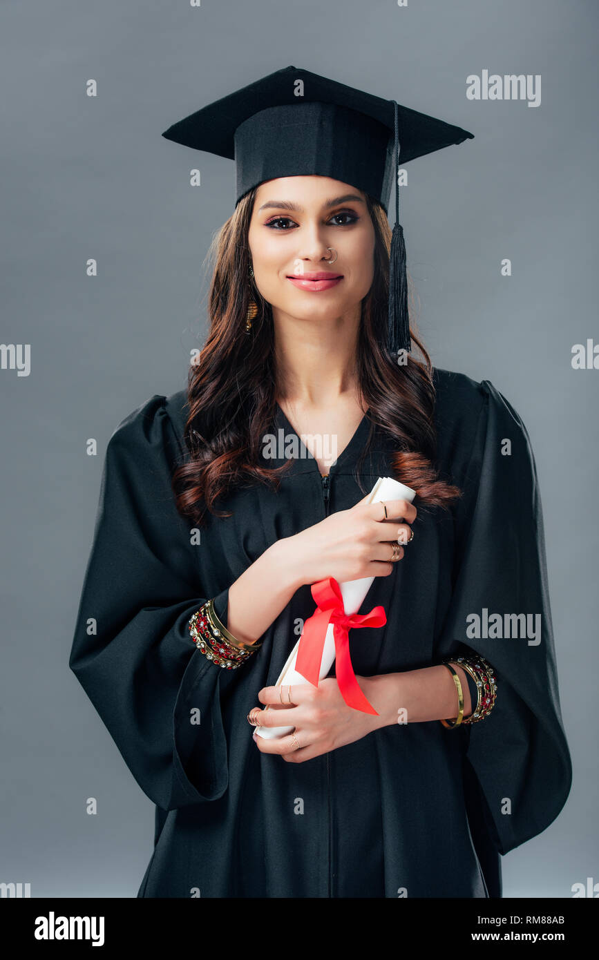 happy female indian student in academic gown and graduation hat holding ...
