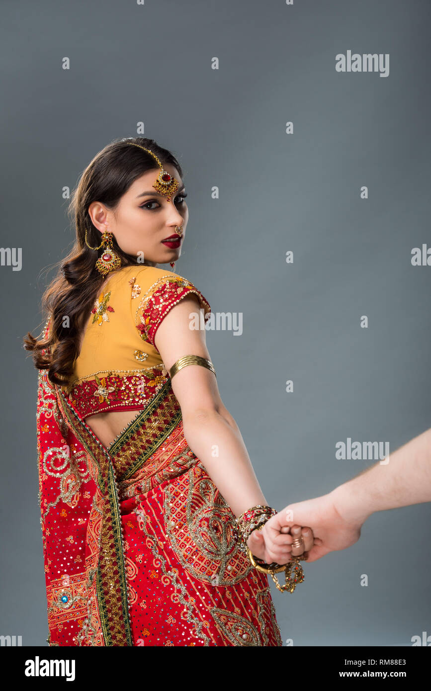 indian couple in traditional clothing holding hands isolated on grey ...