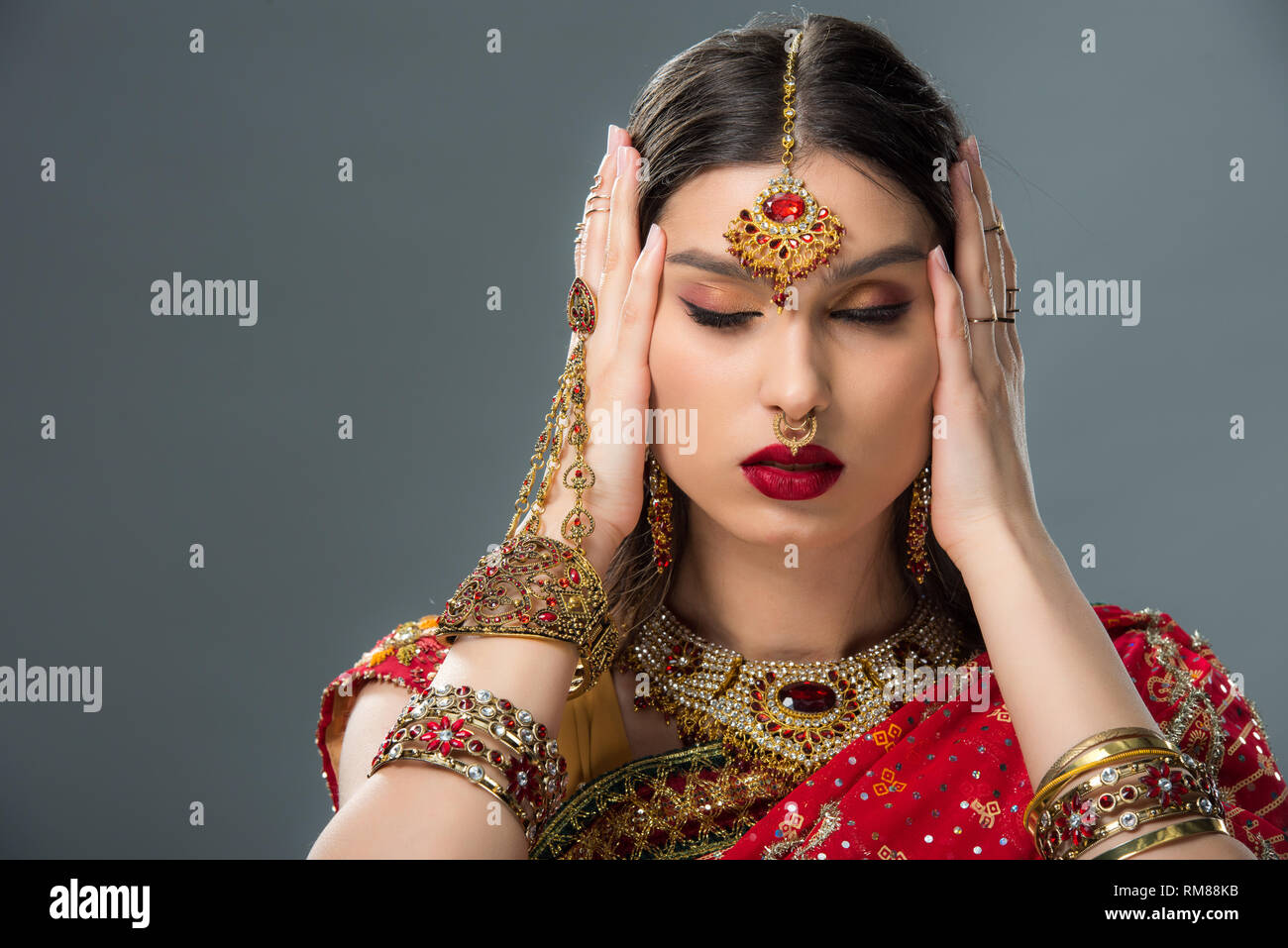 attractive indian woman with bindi touching head, isolated on grey ...