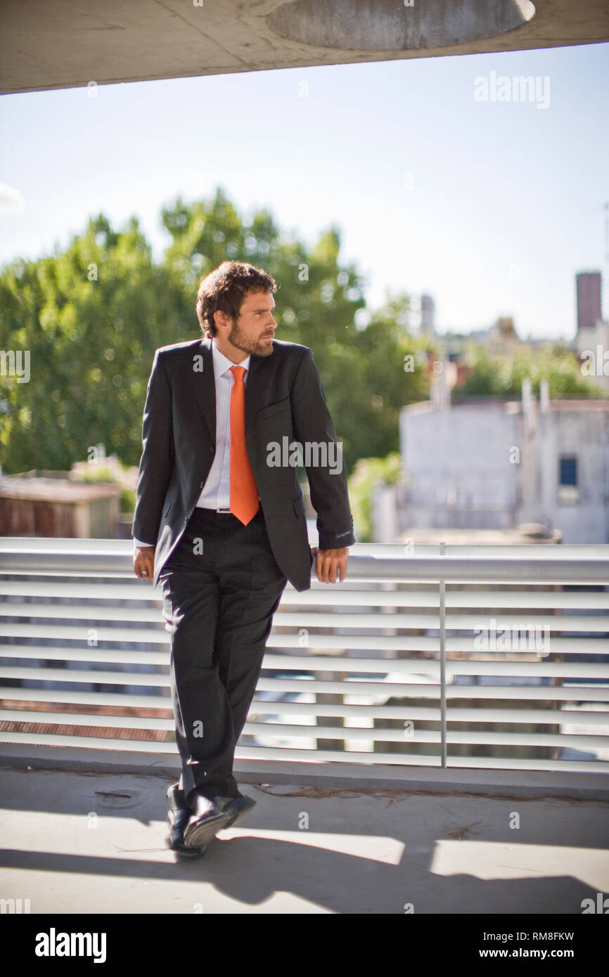 Young adult business man leaning on a balustrade and crossing his legs ...