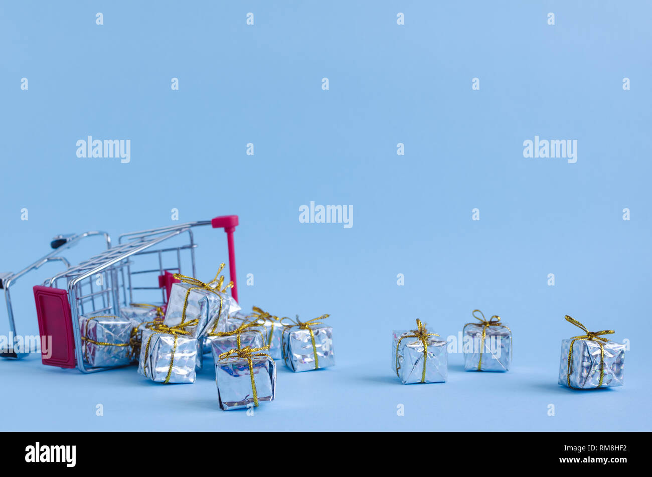 Overturned small shopping cart with presents on blue background ...