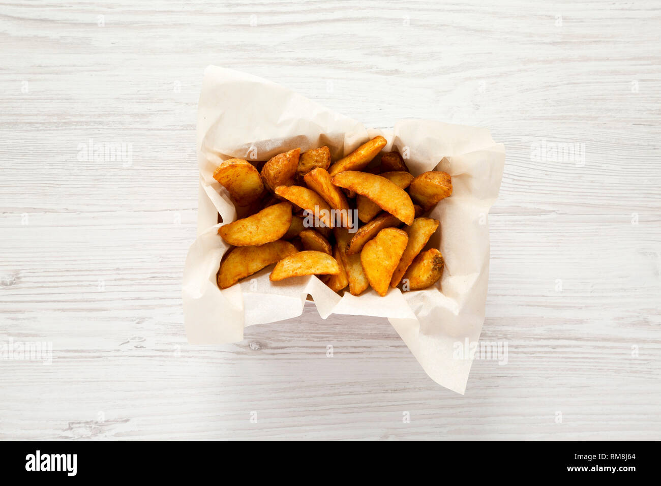 Fried potato wedges in paper box on a white wooden background. Overhead ...