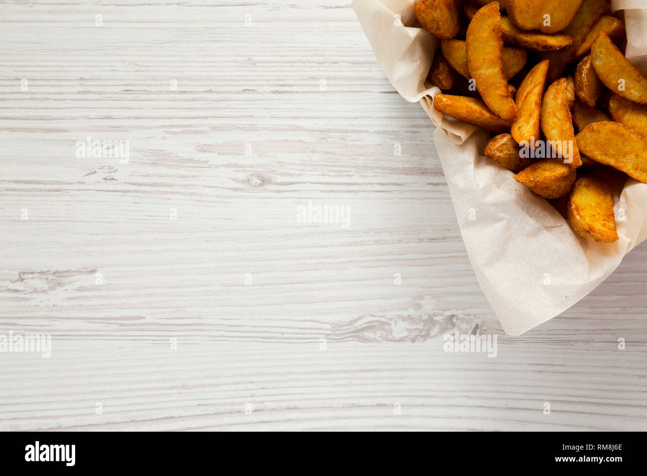 Fried potato wedges in paper box on a white wooden surface. Overhead ...