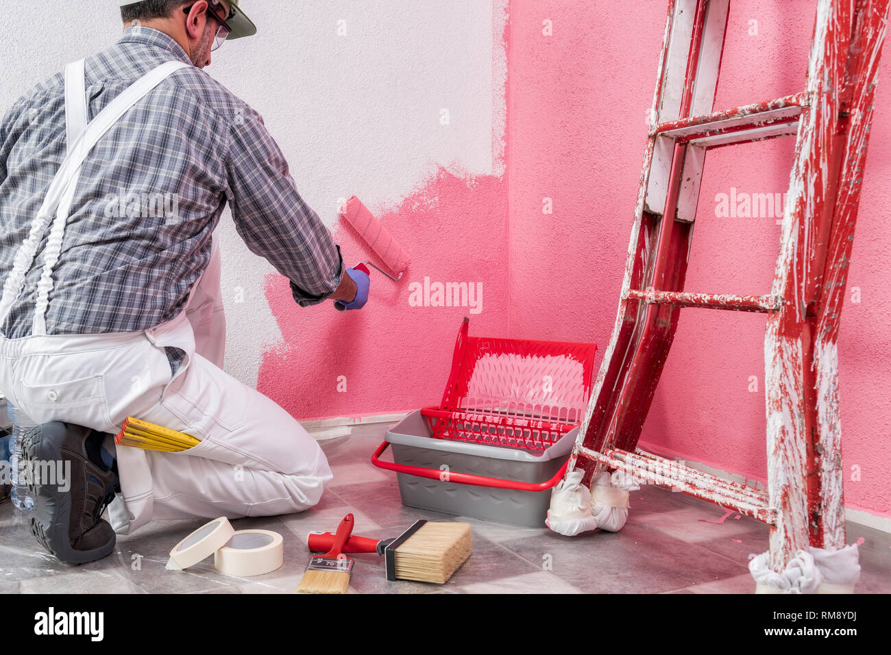 Caucasian house painter worker in white work overalls, with the roller ...