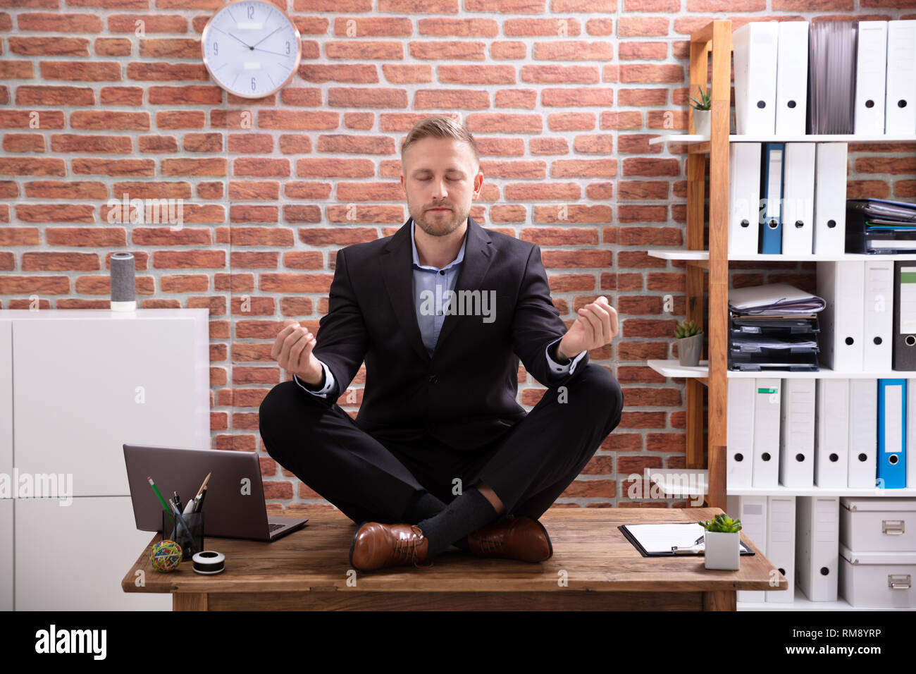 Young Businessman Sitting On Desk Meditating In Office Stock Photo - Alamy