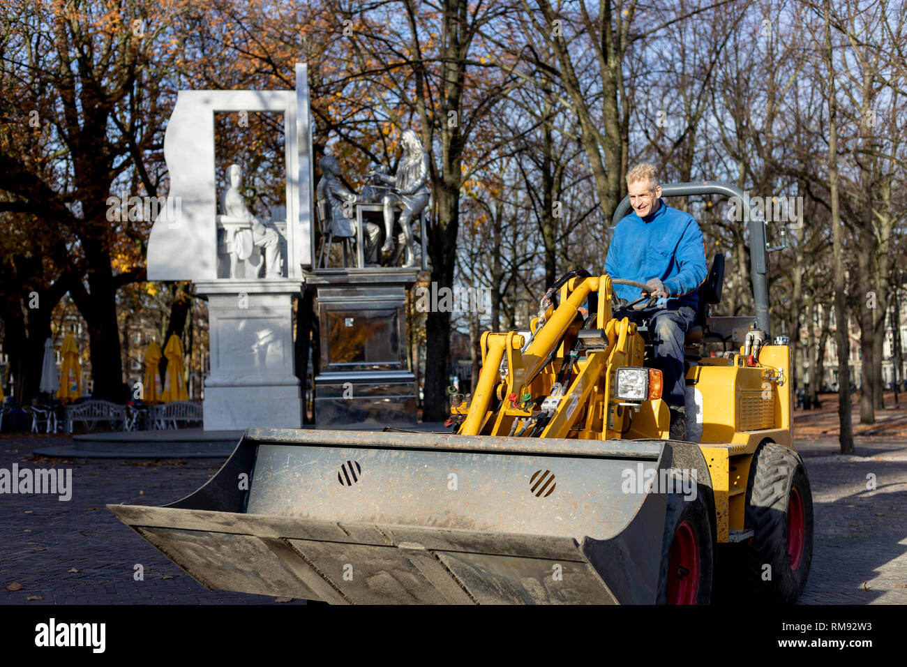 Worker on a dirt digging truck passing a statue in the streets of The ...