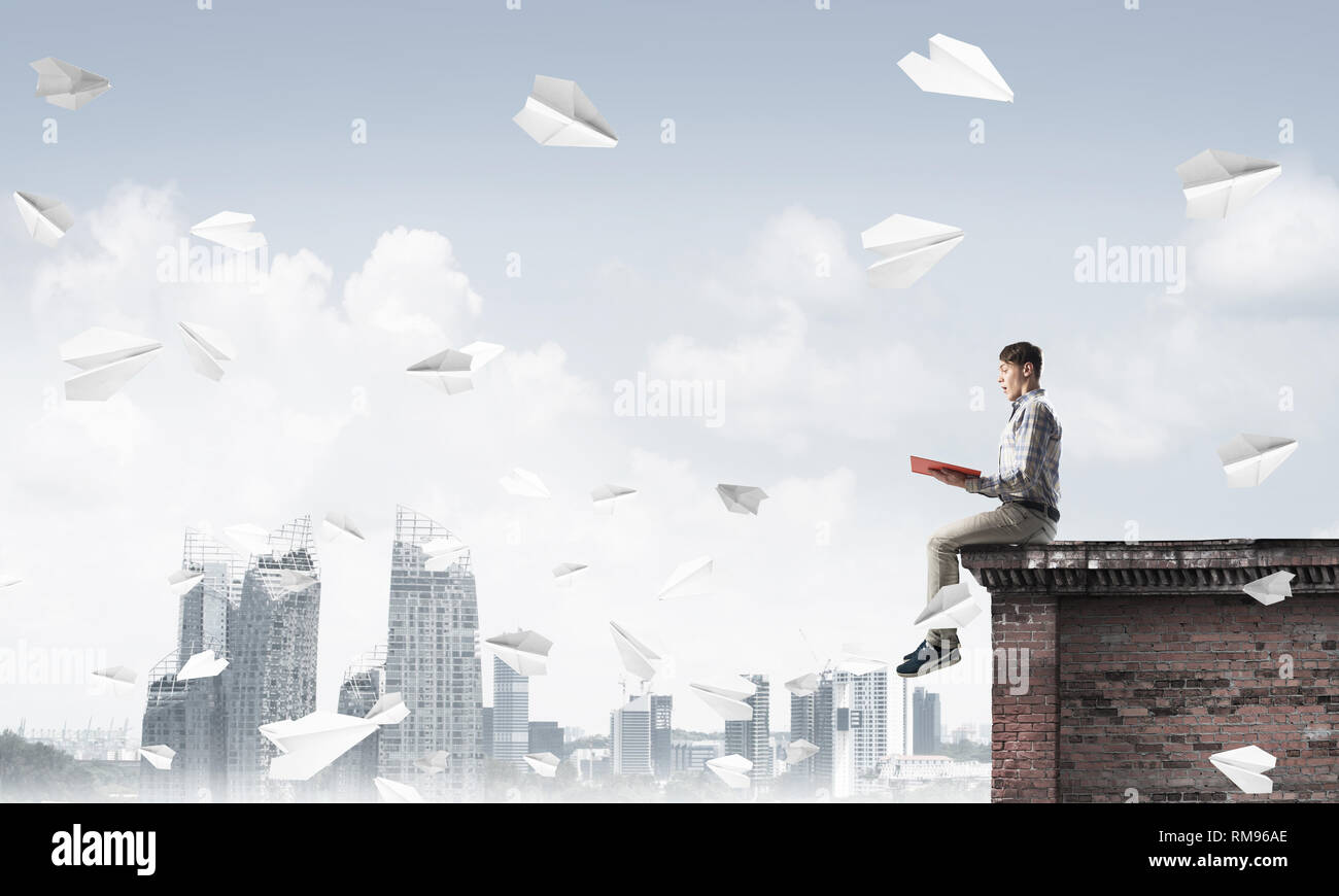 Handsome student guy on roof edge reading book and paper planes fly ...