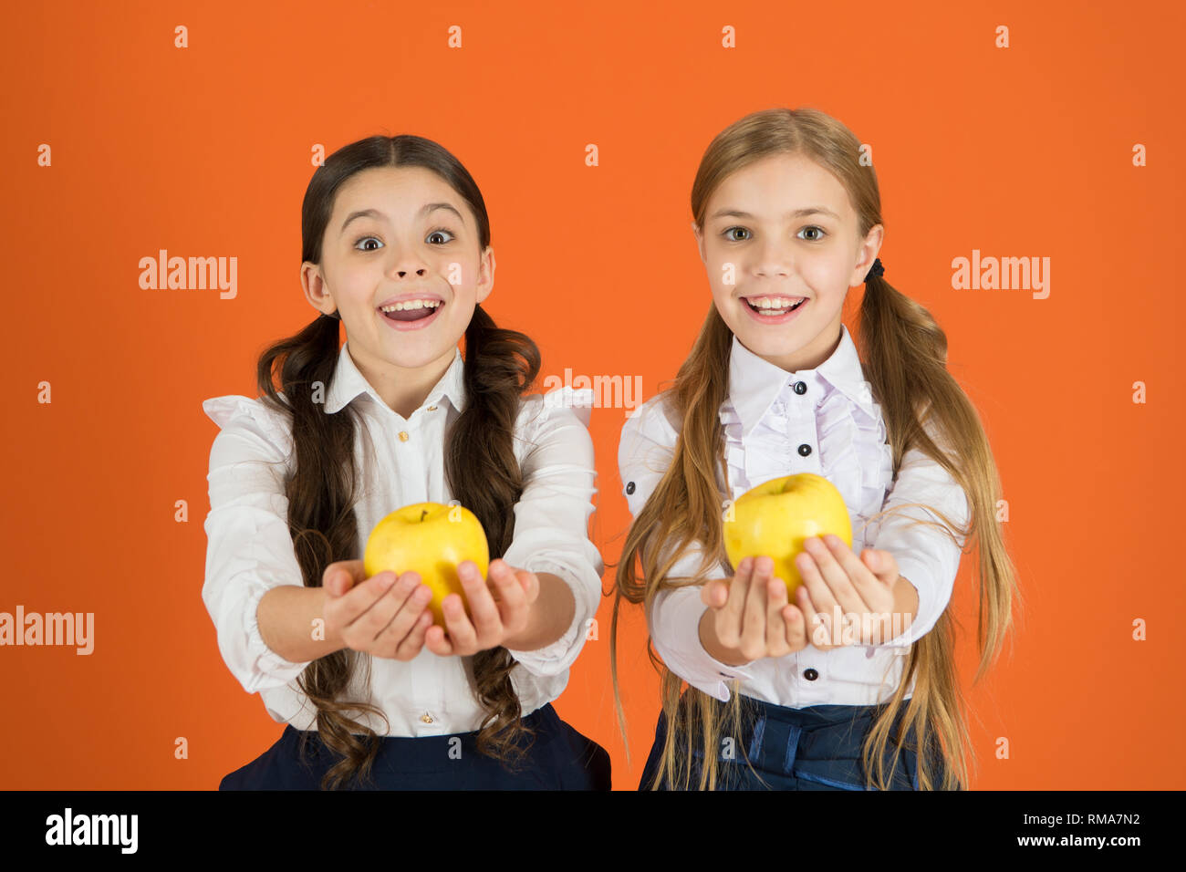 Girls kids school uniform orange background. Schoolgirls eat apples ...