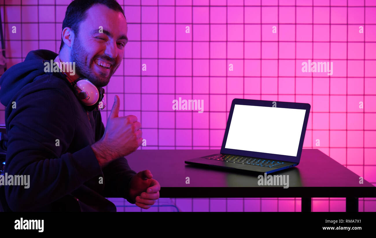 A young cheerful gamer smiling to the camera and looking at laptop ...