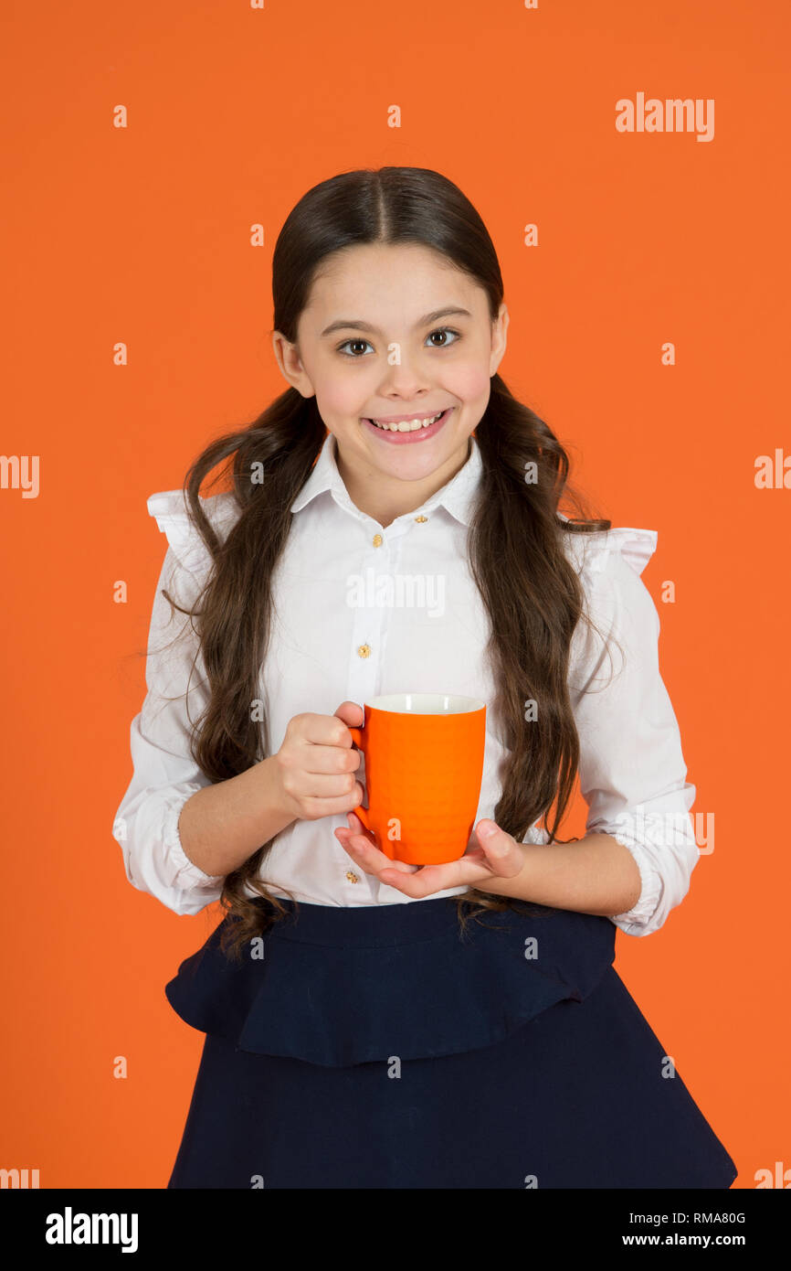 Girl kid school uniform orange background. Schoolgirl hold mug. School ... Girl kid school uniform orange background. Schoolgirl hold mug. School ...