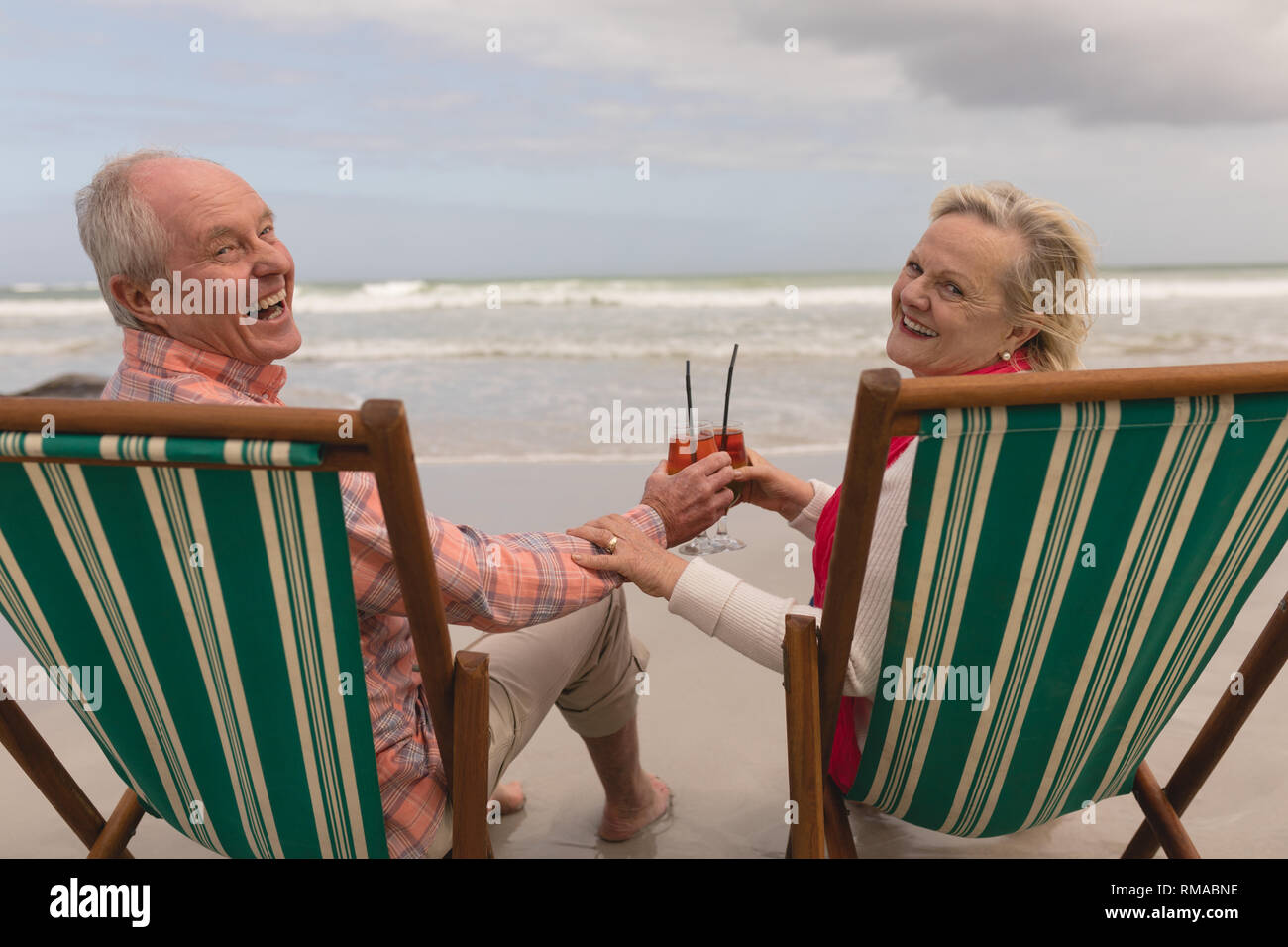 Senior couple toasting glasses of cocktail drinks in a sun lounger ...