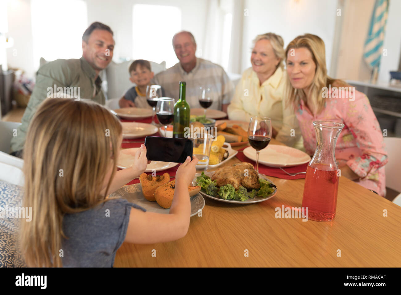 Girl clicking photo of her family with mobile phone on dining table ...