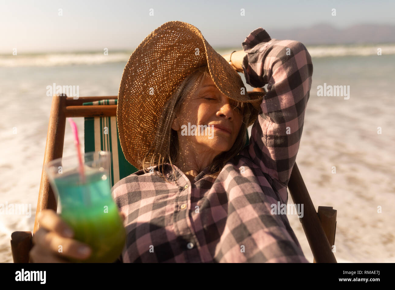 Senior woman having cocktail drink while relaxing on sun lounger at ...