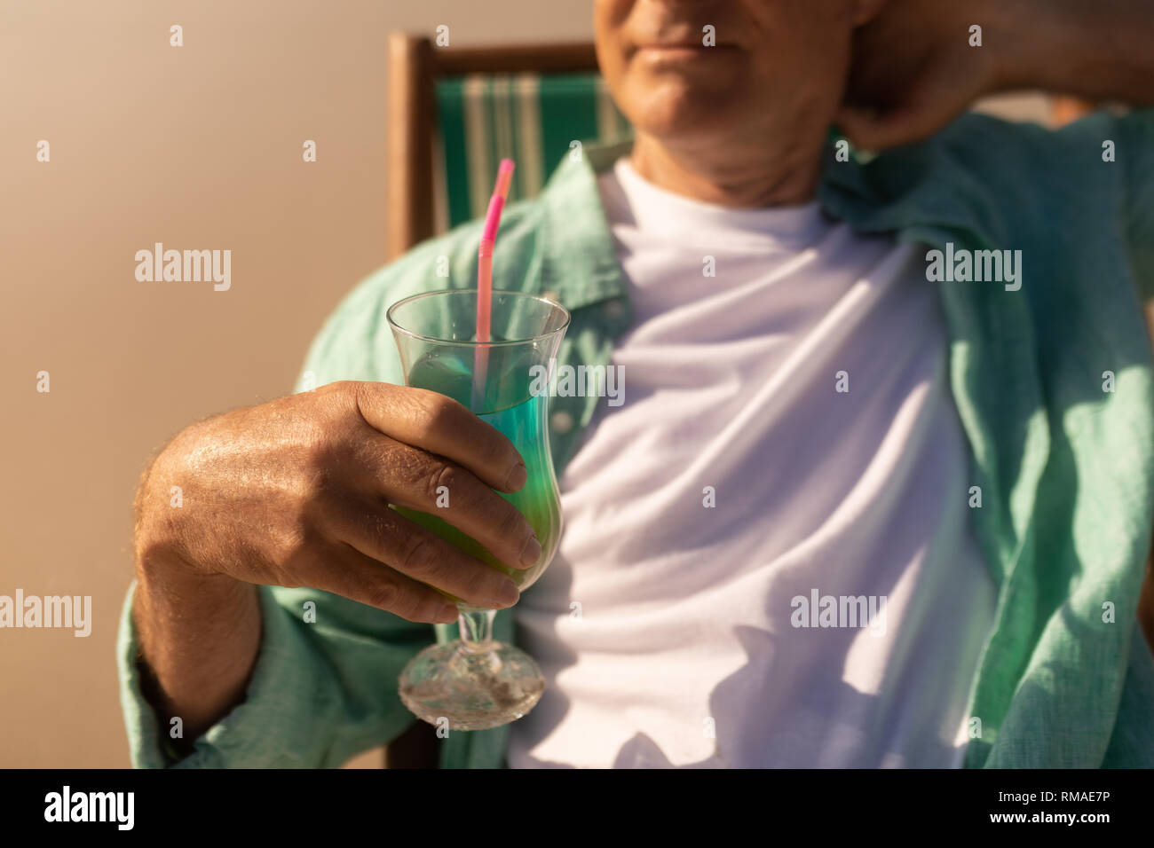 Senior man having cocktail drink while relaxing on sun lounger at beach ...