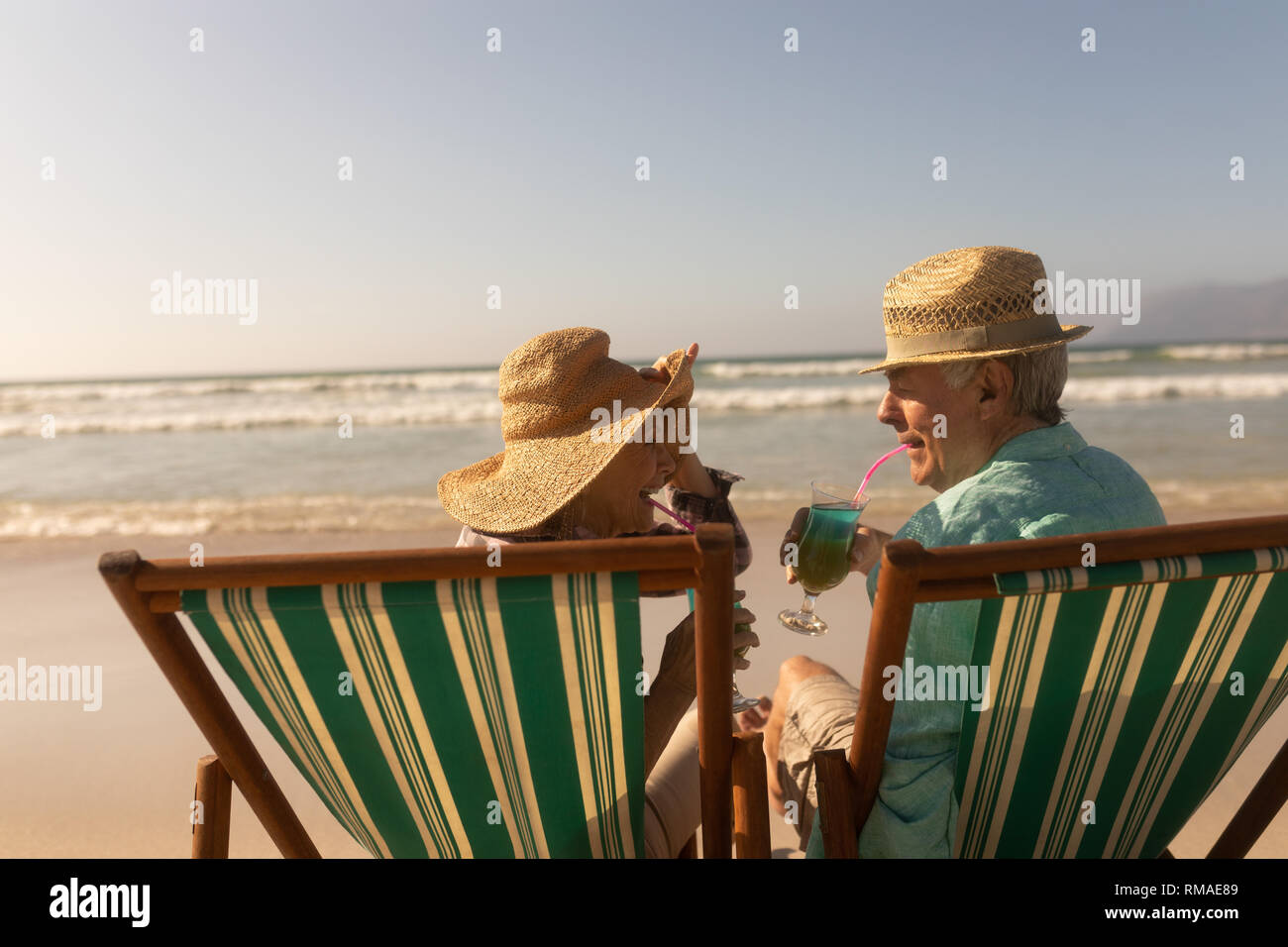 Senior couple having cocktail drink while relaxing on sun lounger at ...