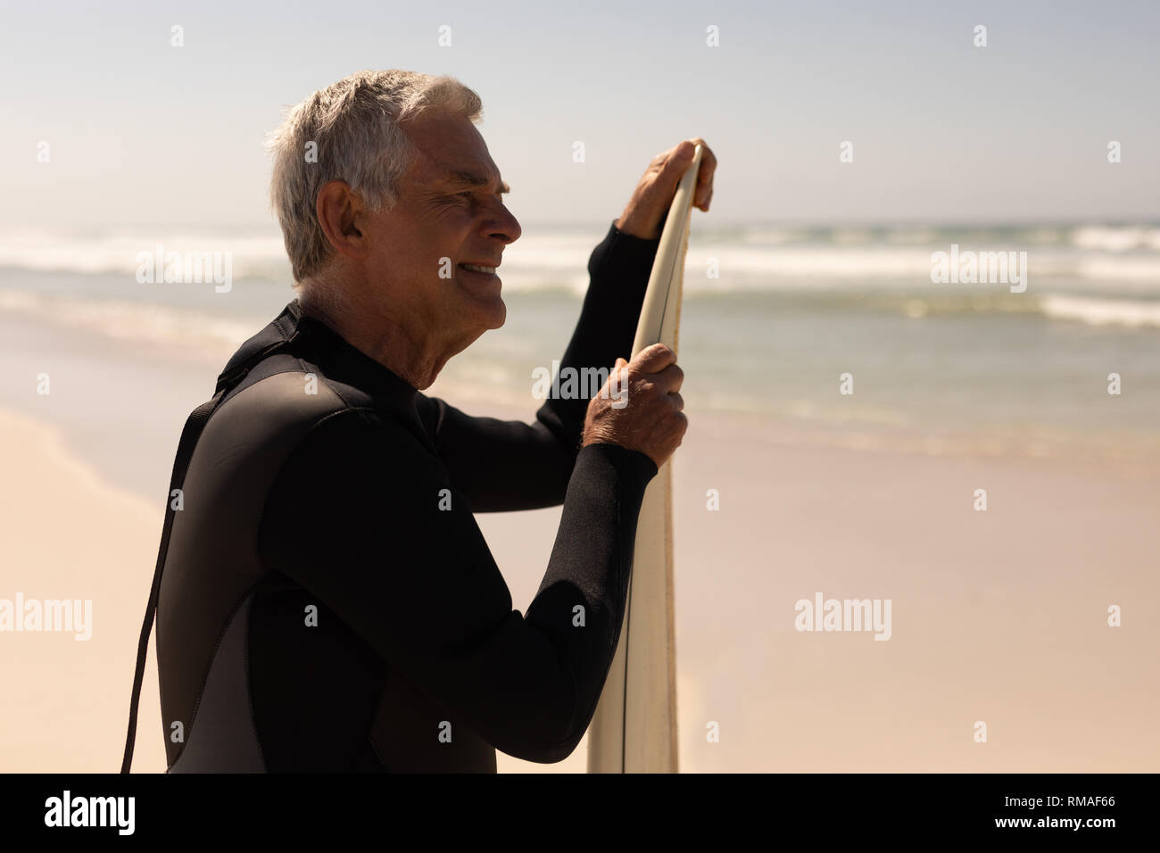 Side view of senior male surfer standing with surfboard on the beach ...