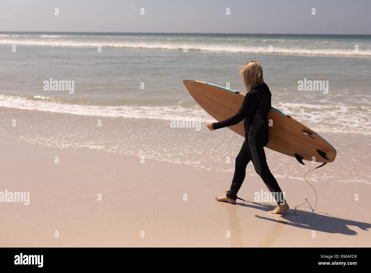 Side view of senior female surfer walking with surfboard on the beach ...