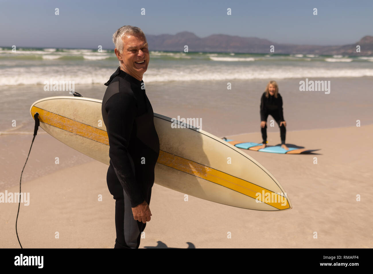 Side view of senior surfer couple standing with surfboard on the beach ...