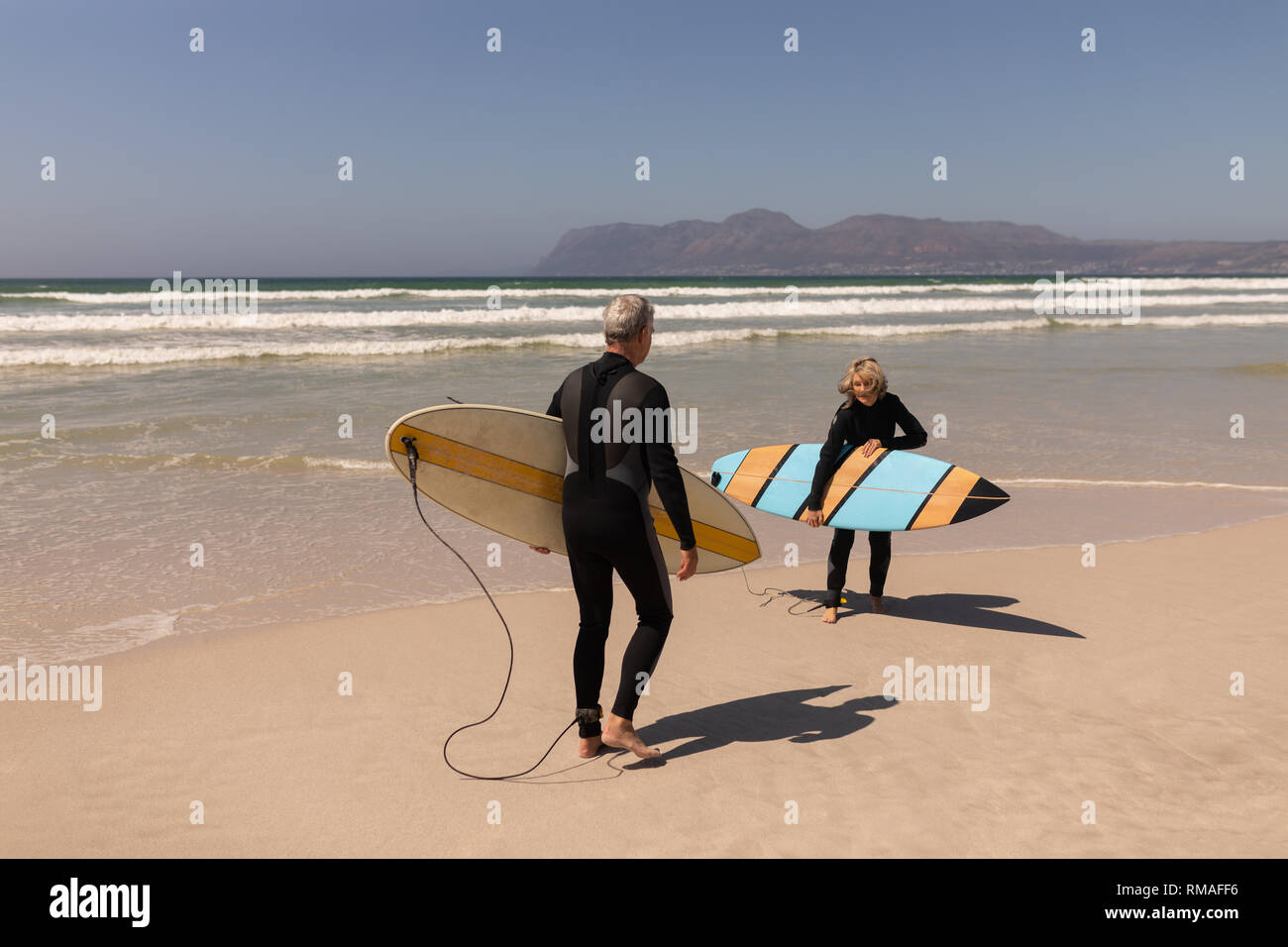 Side view of senior surfer couple standing with surfboard on the beach ...