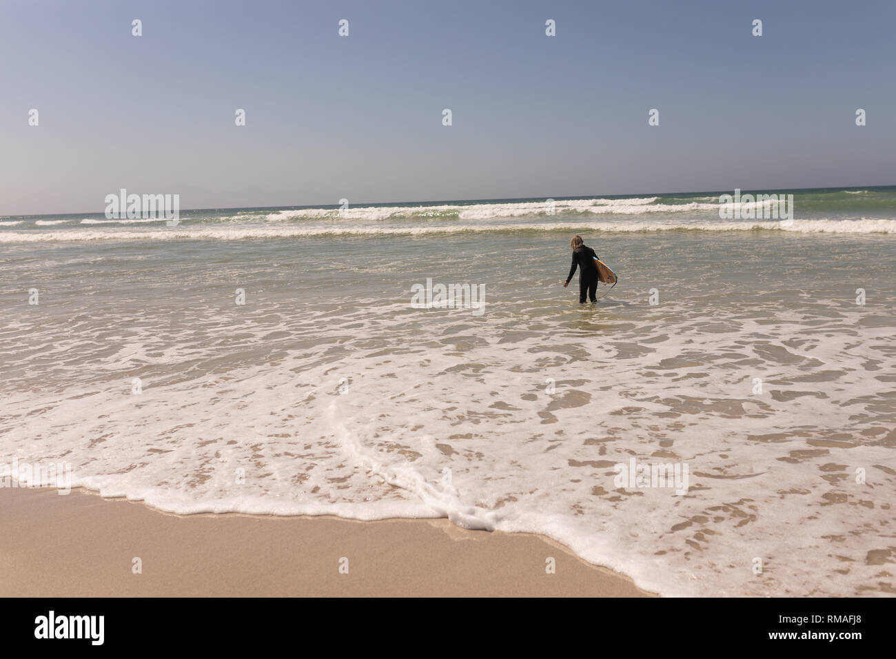 Side view of senior female surfer standing with surfboard on the beach ...