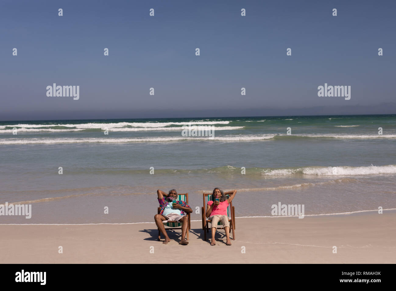 Senior couple relaxing on sun lounger and drinking cocktail on beach ...
