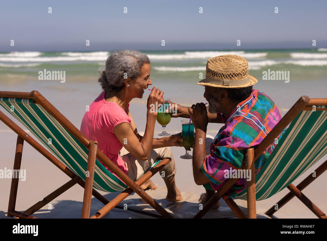 Senior couple relaxing on sun lounger and drinking cocktail on beach ...