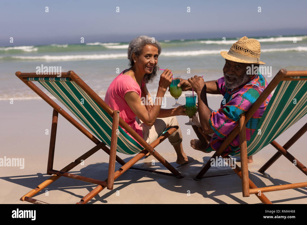 Senior couple relaxing on sun lounger and drinking cocktail on beach ...