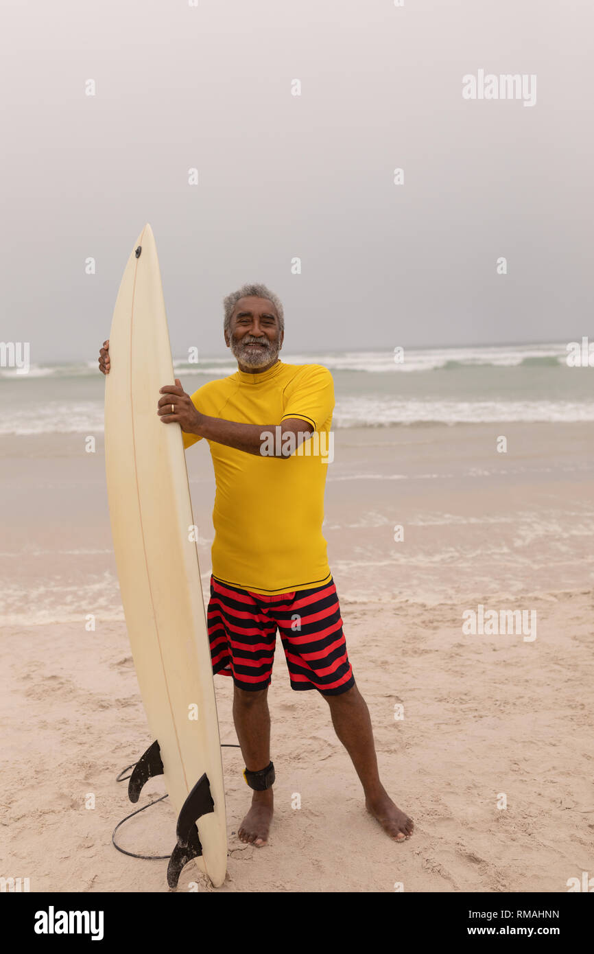 Happy senior male surfer standing with surfboard and looking at camera ...