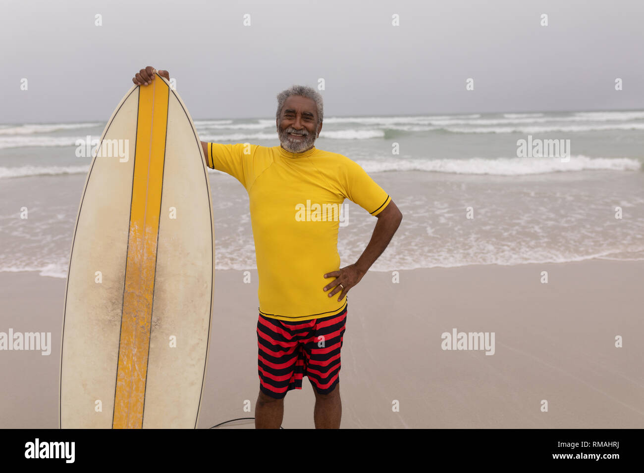 Senior male surfer standing with surfboard and looking at camera on the ...