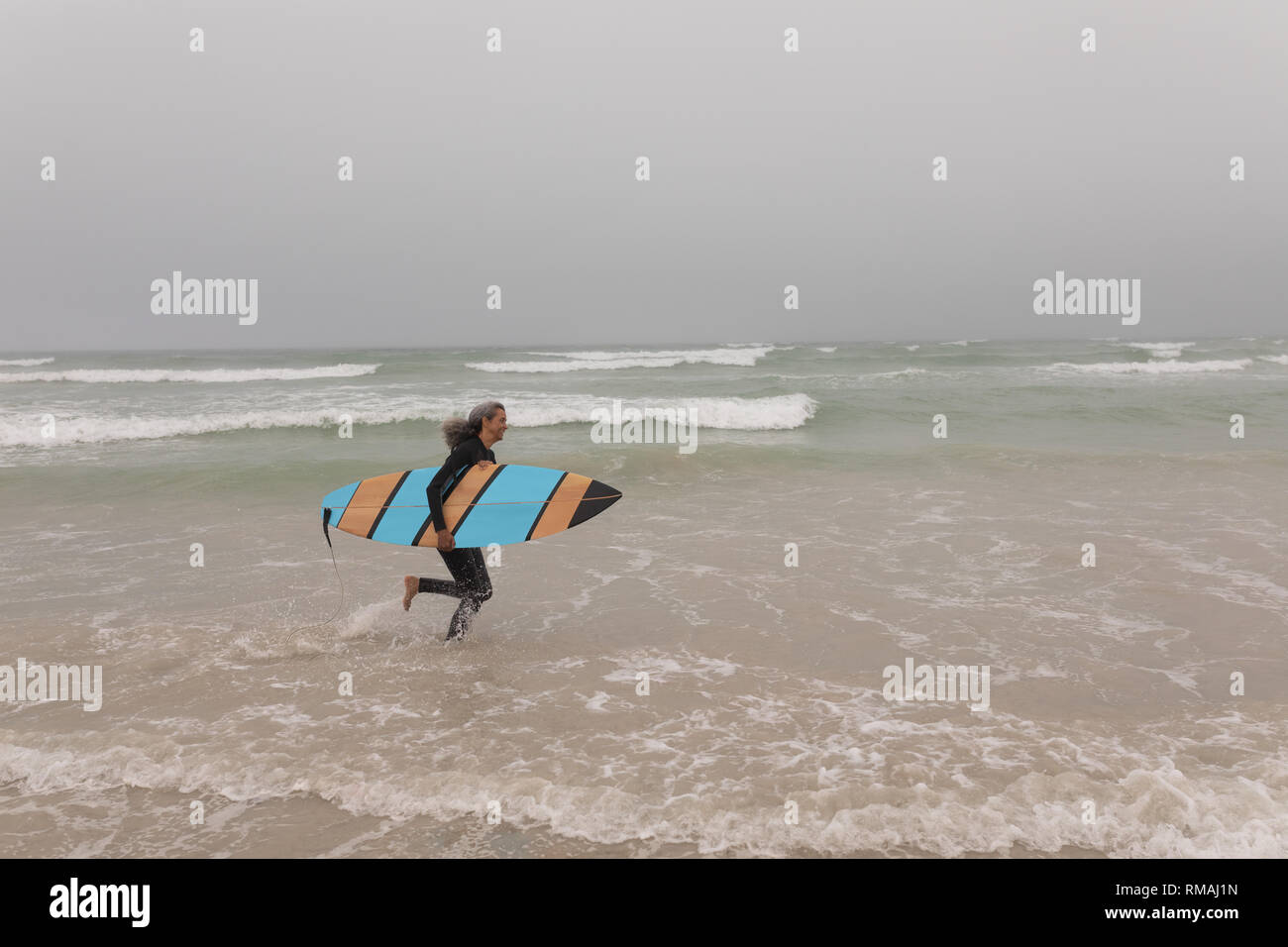 Senior female surfer with surfboard running on the beach Stock Photo ...