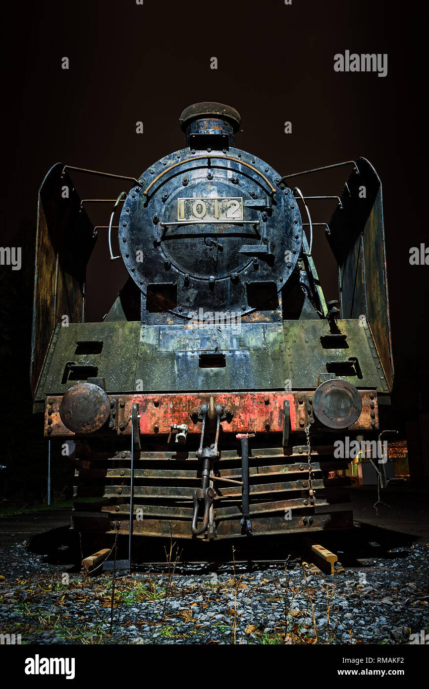 An old steam engine stands on the railroad tracks on an autumn night at ...