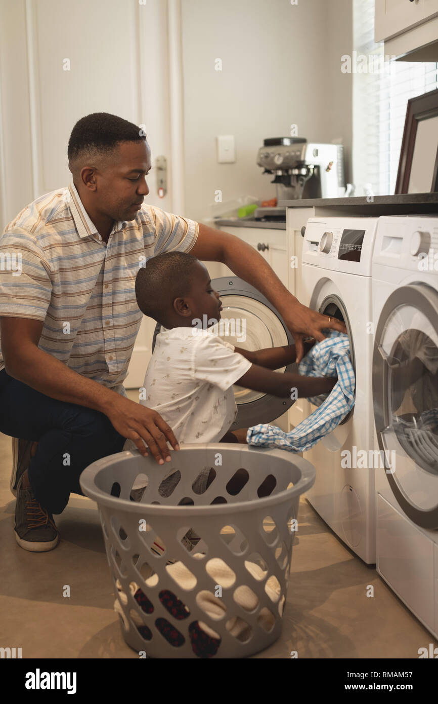 African American father and son washing clothes in washing machine ...