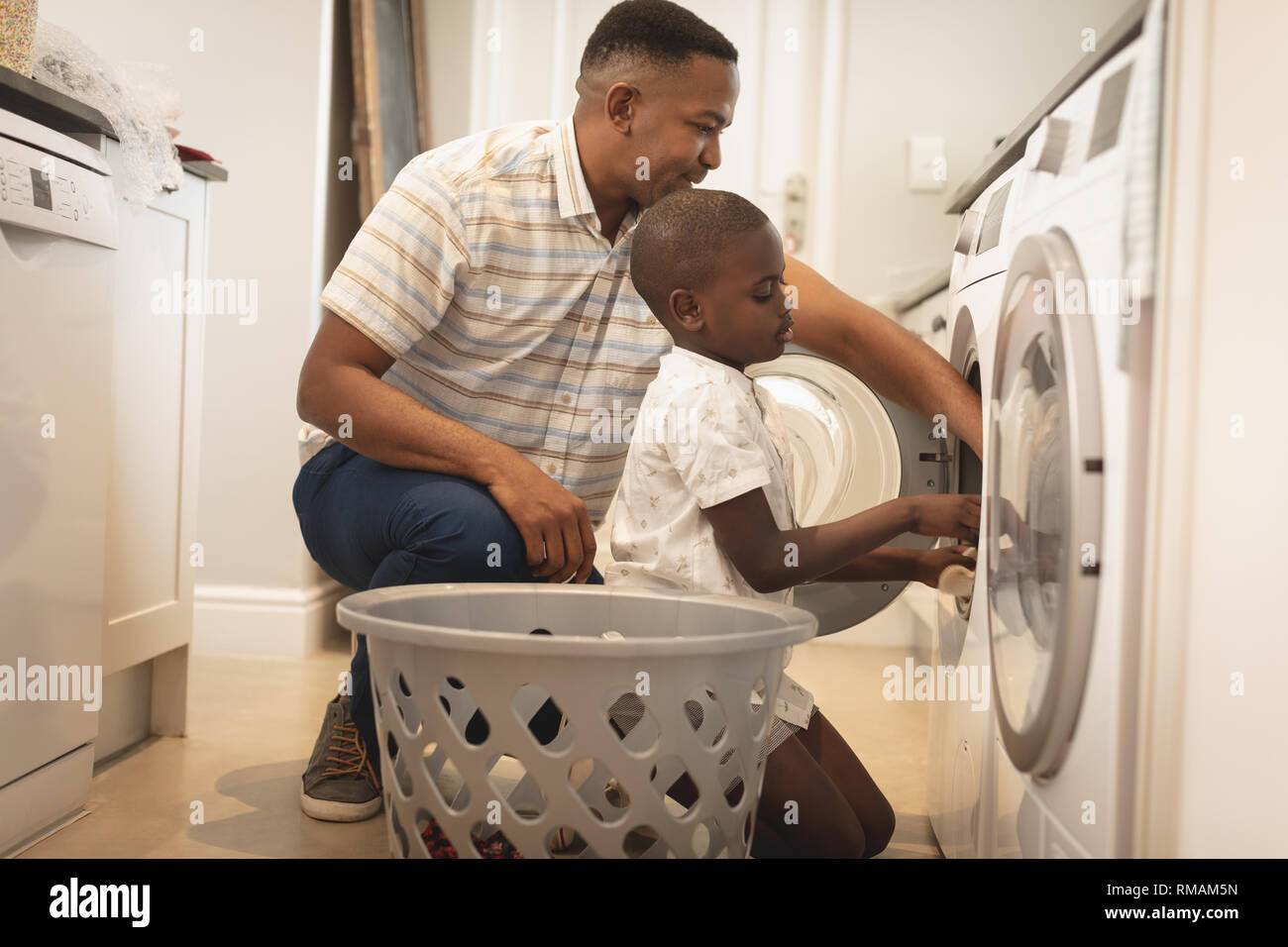 African American father and son washing clothes in washing machine ...