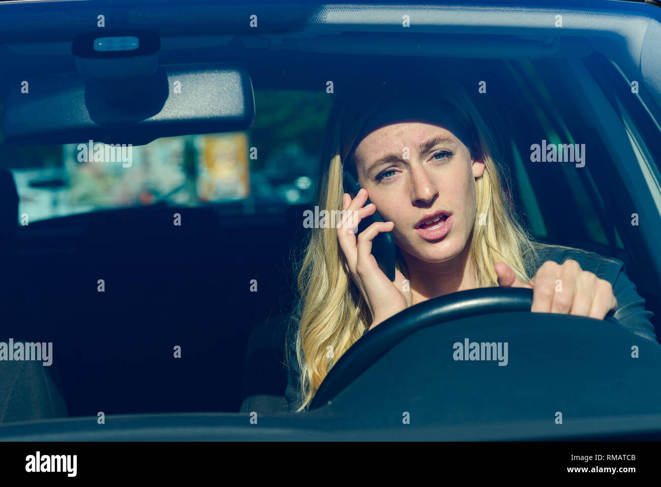 Front view of young blond woman talking on phone while driving car ...