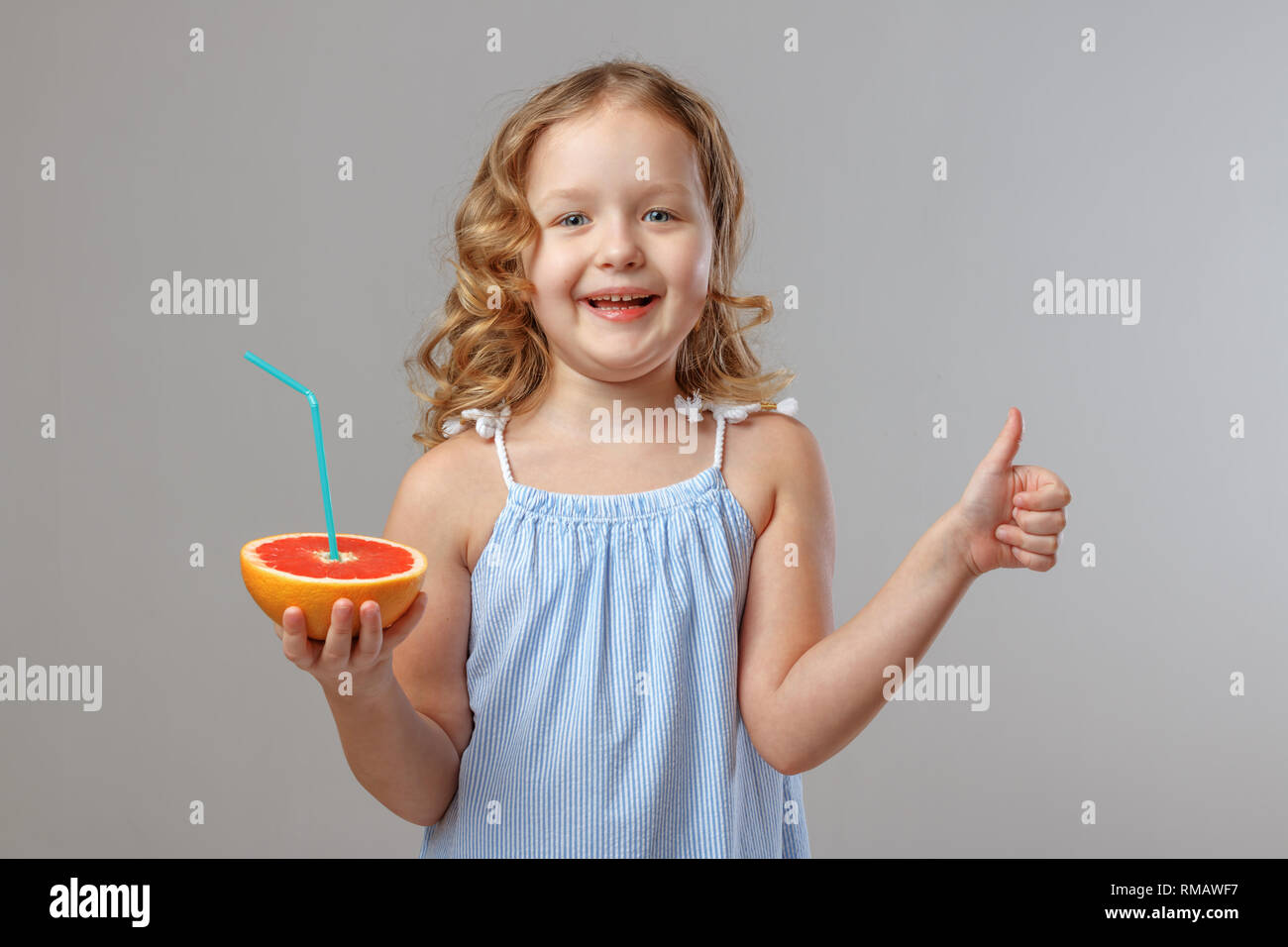 Happy little girl child holds half a grapefruit with a straw and shows ...