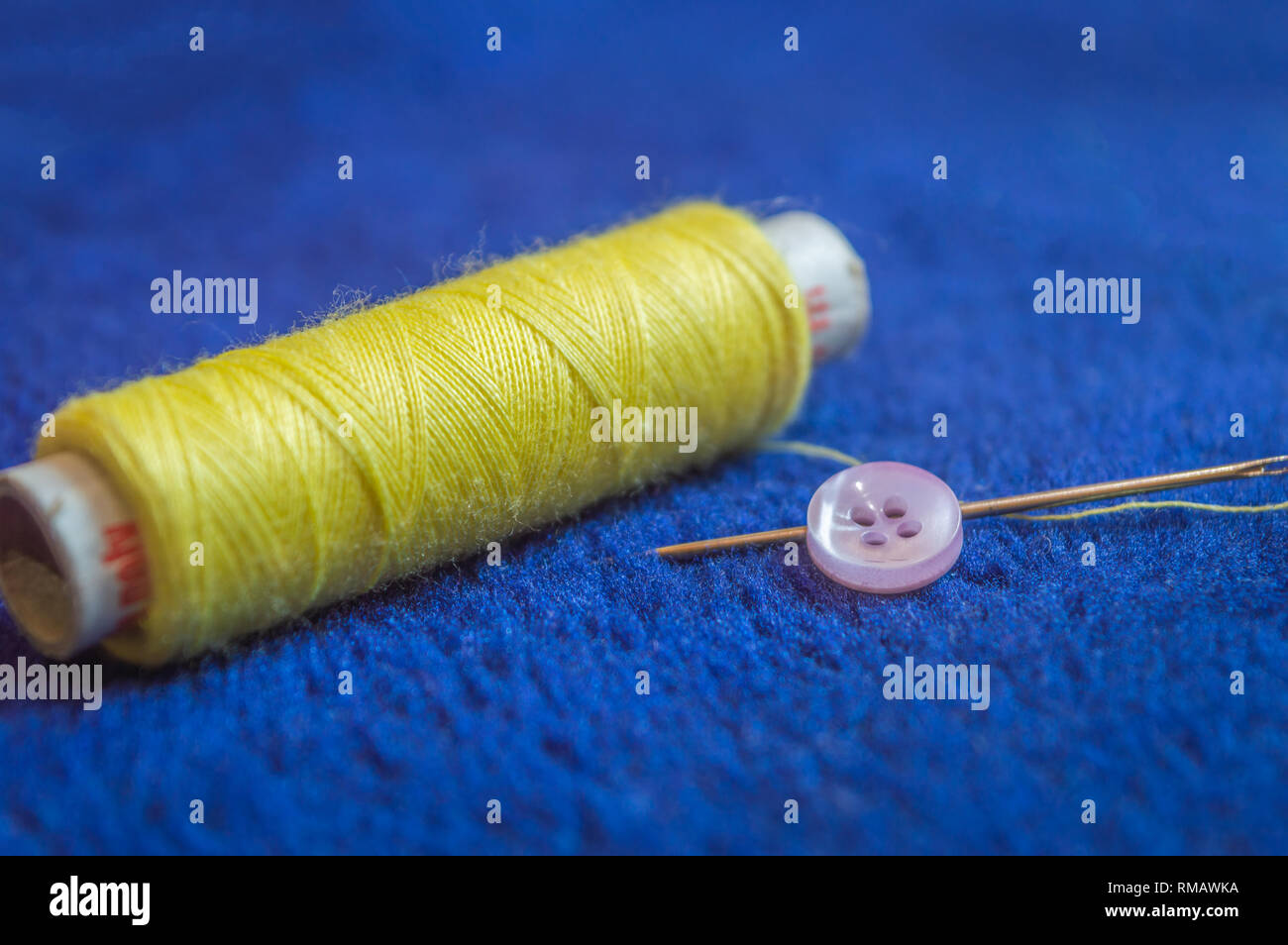 A yellow thread roll with a needle and a button on a blue background ...