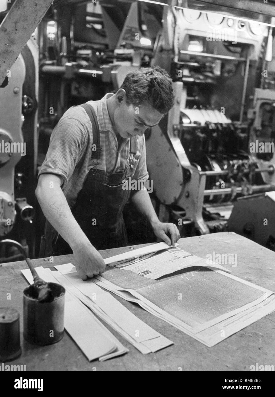 A worker makes an adjustment behind the printing plate, so that a ...