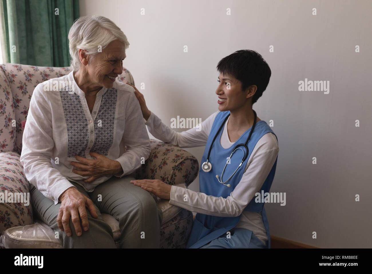 Female doctor interacting with senior woman in living room Stock Photo ...