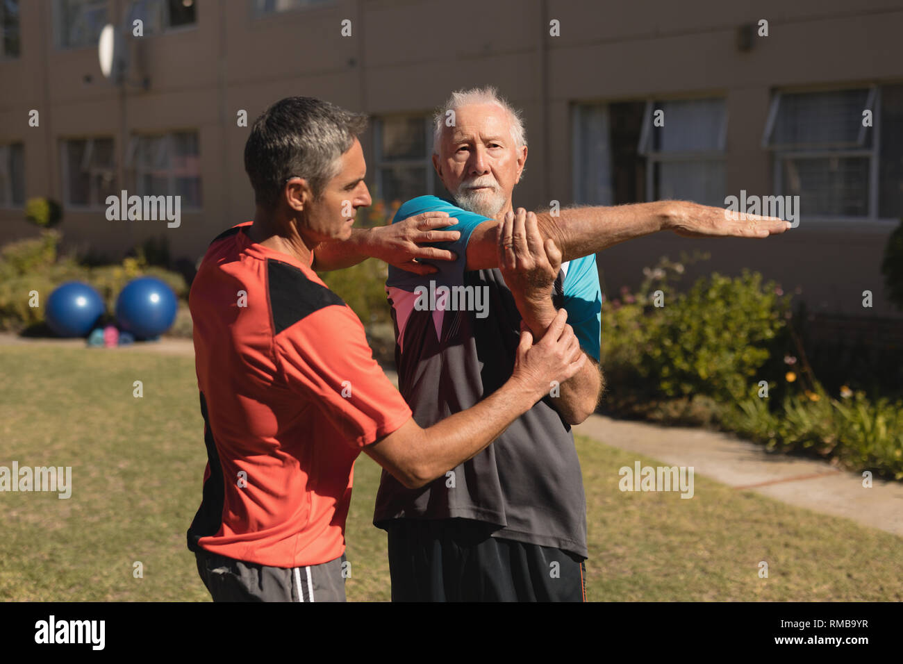 Trainer assisting senior man in performing exercise Stock Photo - Alamy